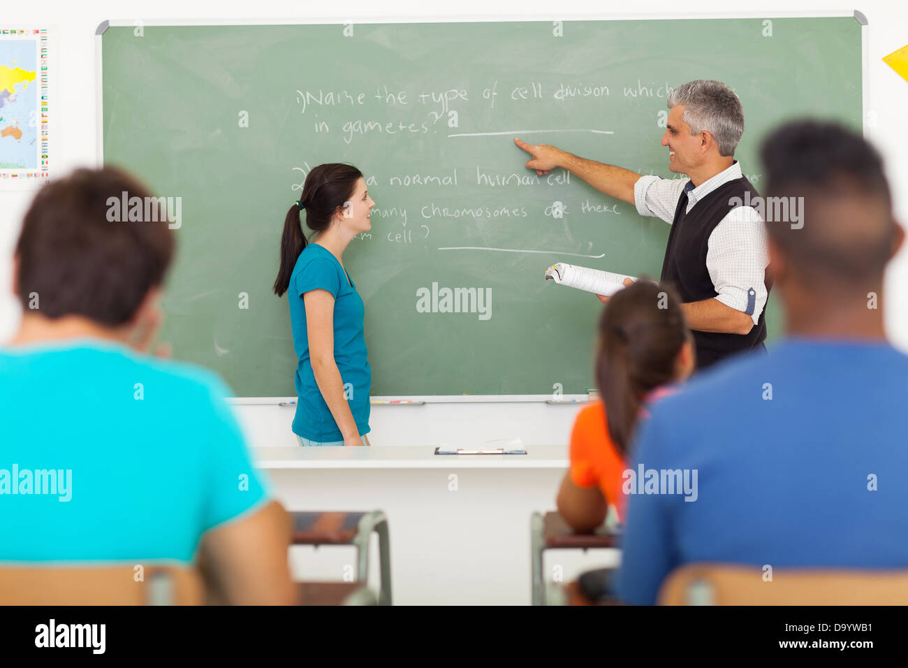 senior teacher pointing at chalkboard with student standing in front of ...