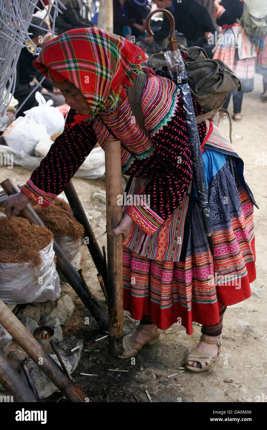 Colorfully dressed Flower Hmong woman smoking traditional bamboo pipe ...