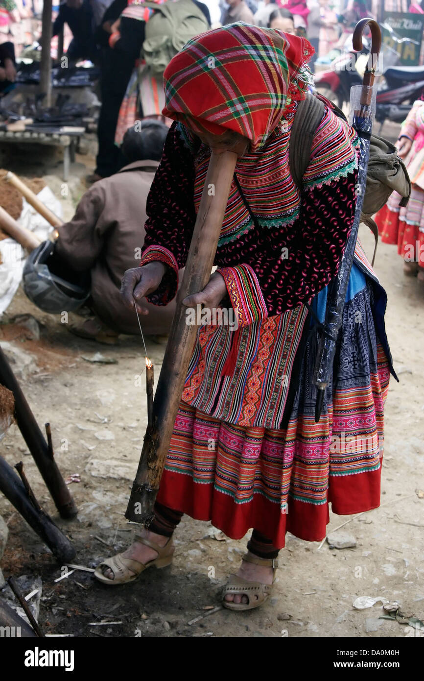 Colorfully dressed Flower Hmong woman smoking traditional bamboo pipe ...