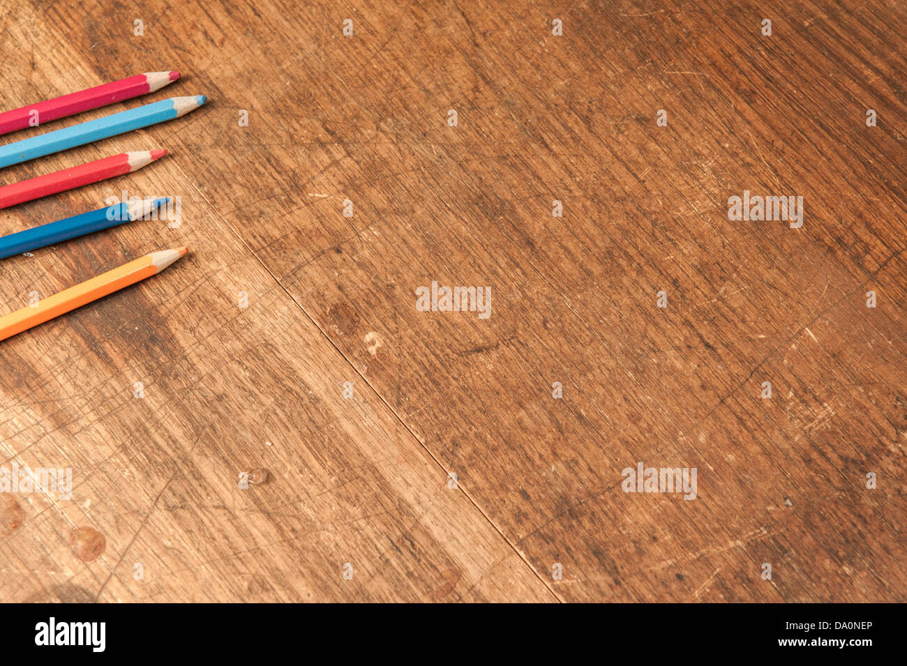 Scratched and worn timber table top with coloured pencils on the side ...