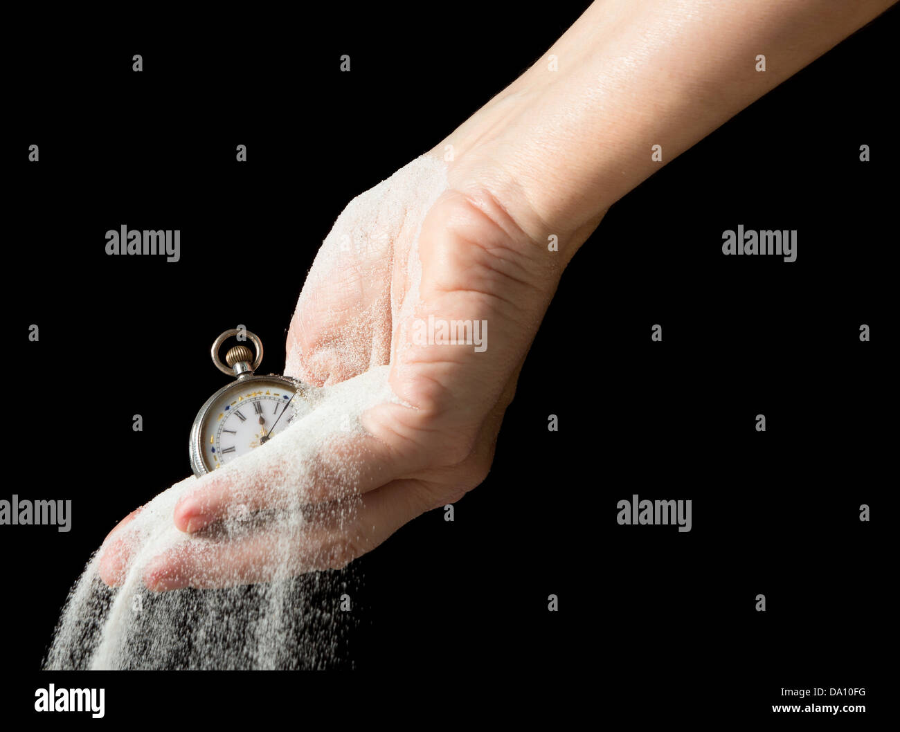 Sand flowing between fingers of a hand holding an antique pocket watch ...