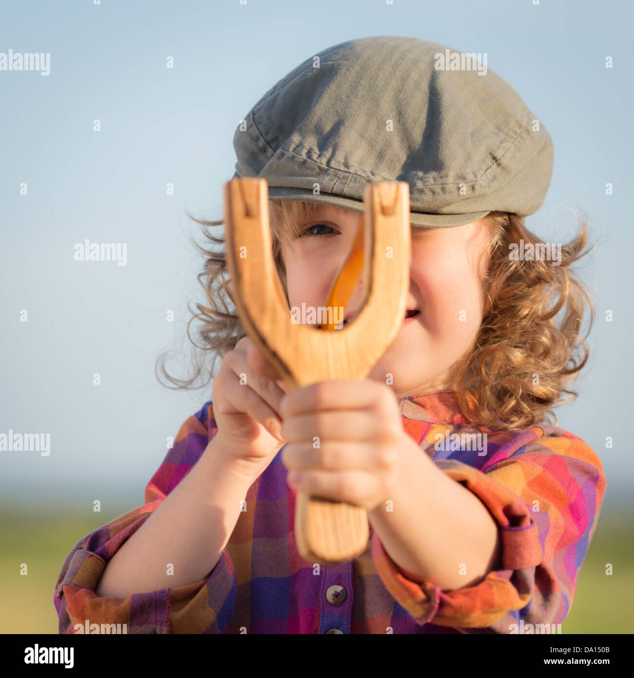 Funny kid shooting wooden slingshot against blue summer sky background ...