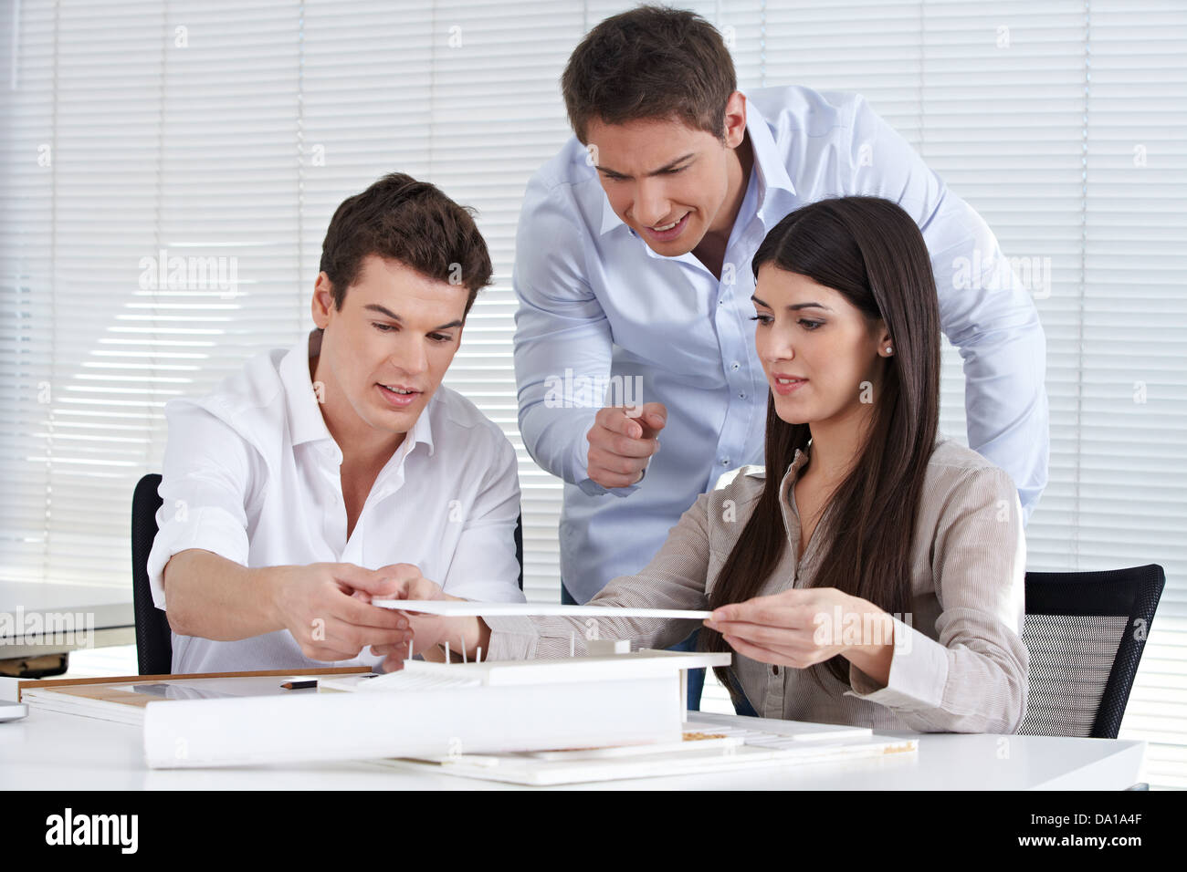 Three architects in an office creating a house model together Stock ...