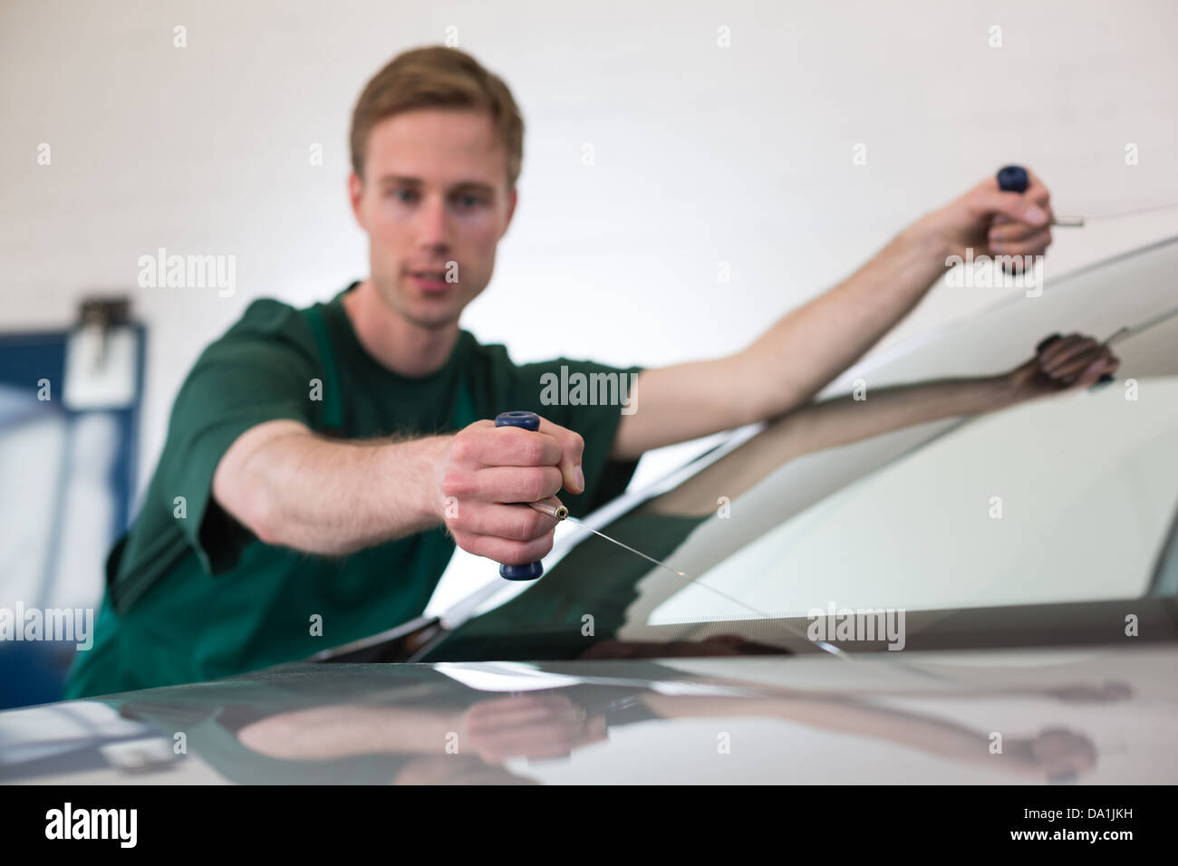 Glazier cutting adhesive of windscreen with a wire to replace ...