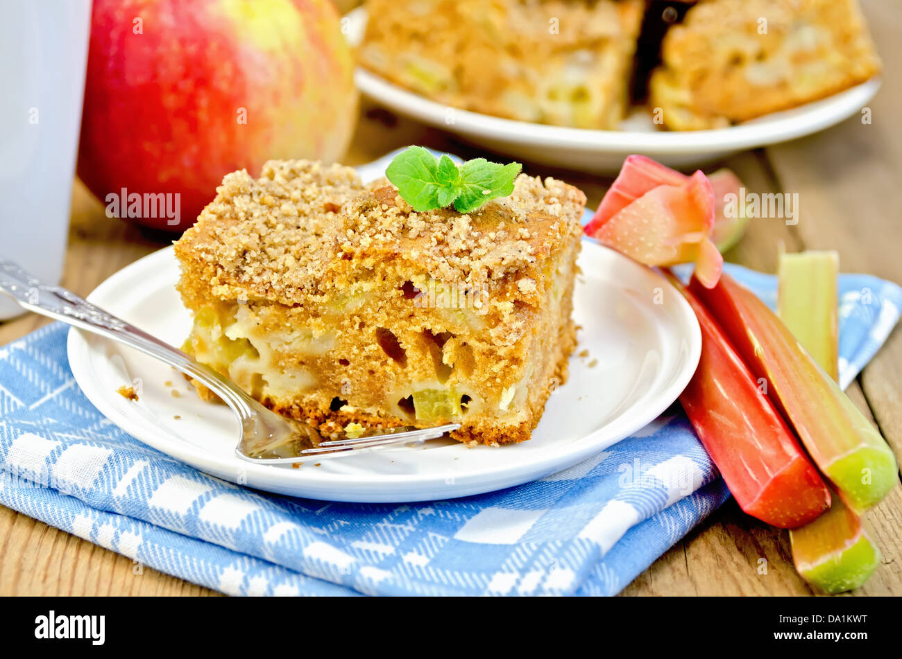 A piece of sweet cake with rhubarb and apples, mint, blue napkin, cup ...