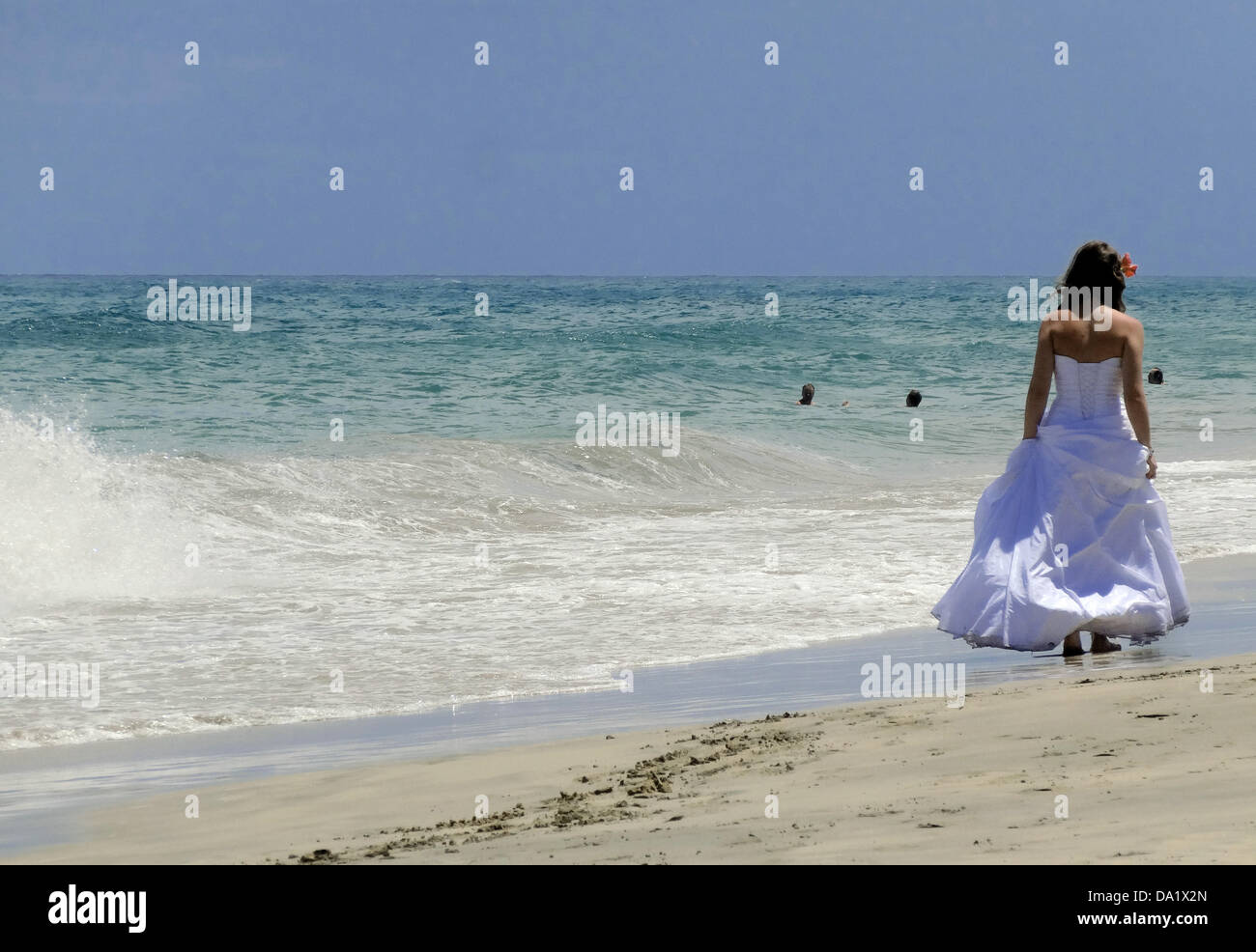 A woman in a wedding dress walks along the sandy beach of Costa Calma ...