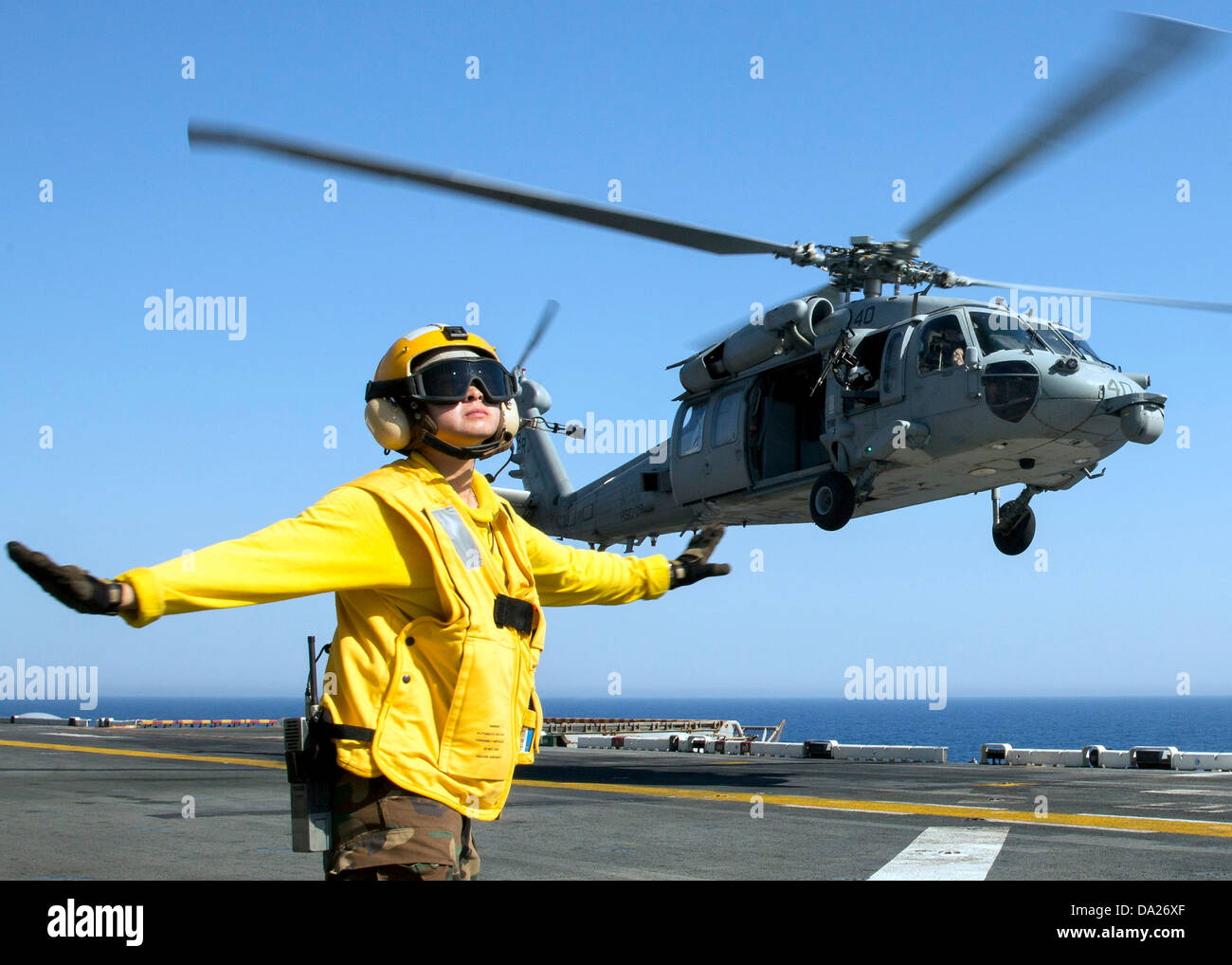 A US sailor signals a MH-60S Sea Hawk helicopter to take off from the ...