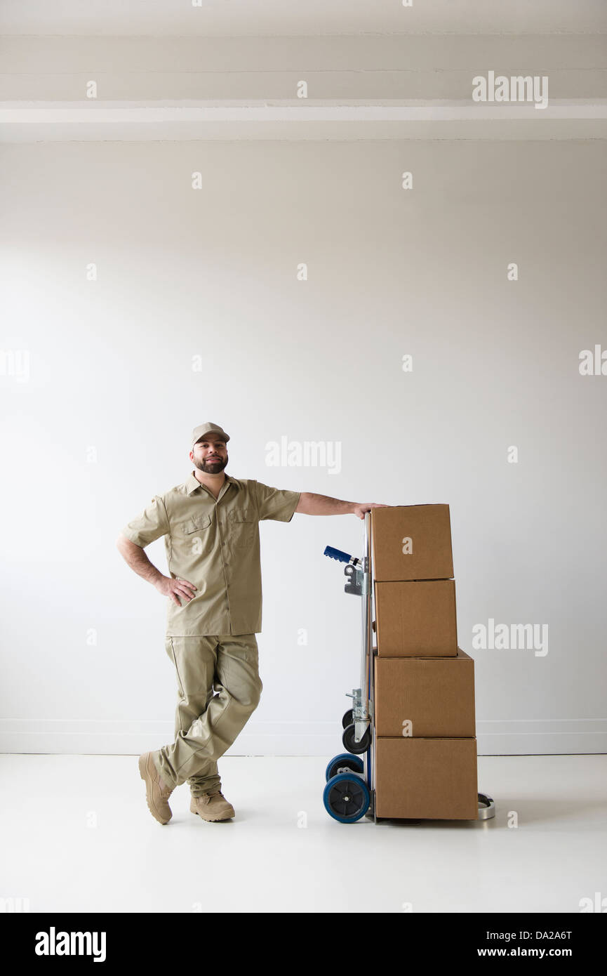Portrait of delivery man standing next to push cart Stock Photo - Alamy