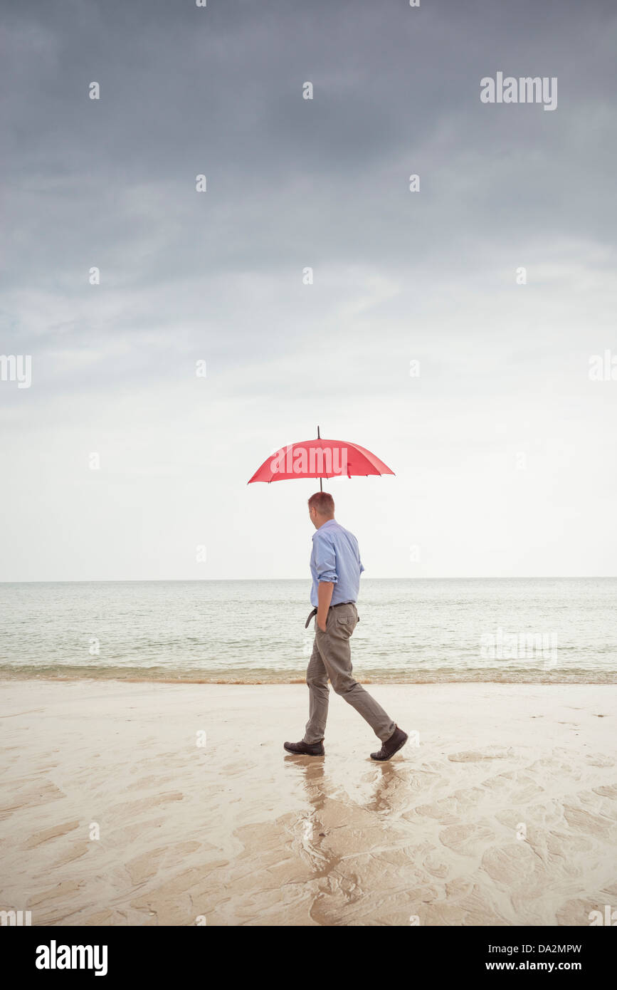 Solitude, Man in his early 40's walks on empty beach with Umbrella ...