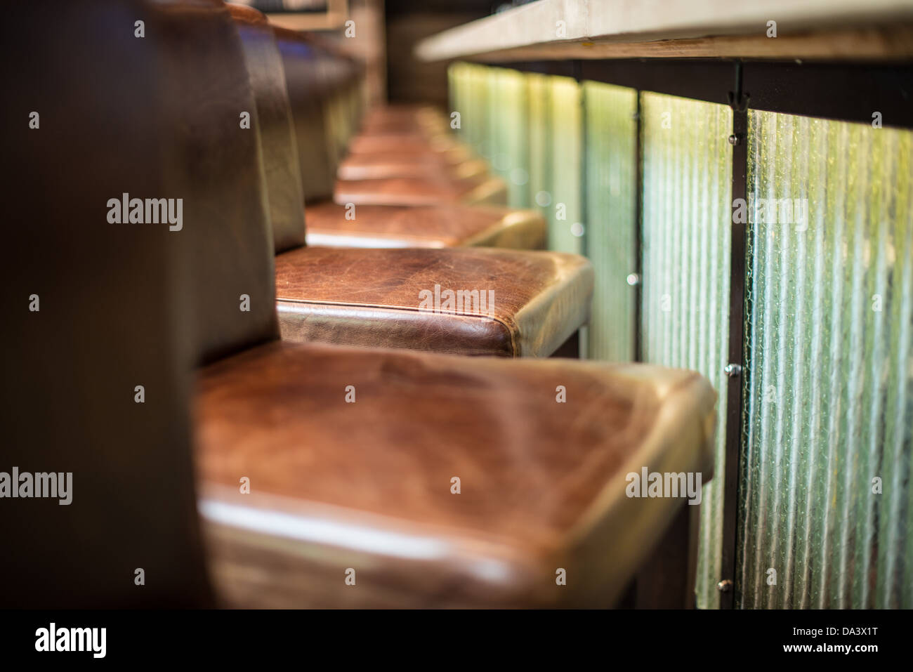 A row of brown leather bar stool chairs lined up next to a bar at a ...