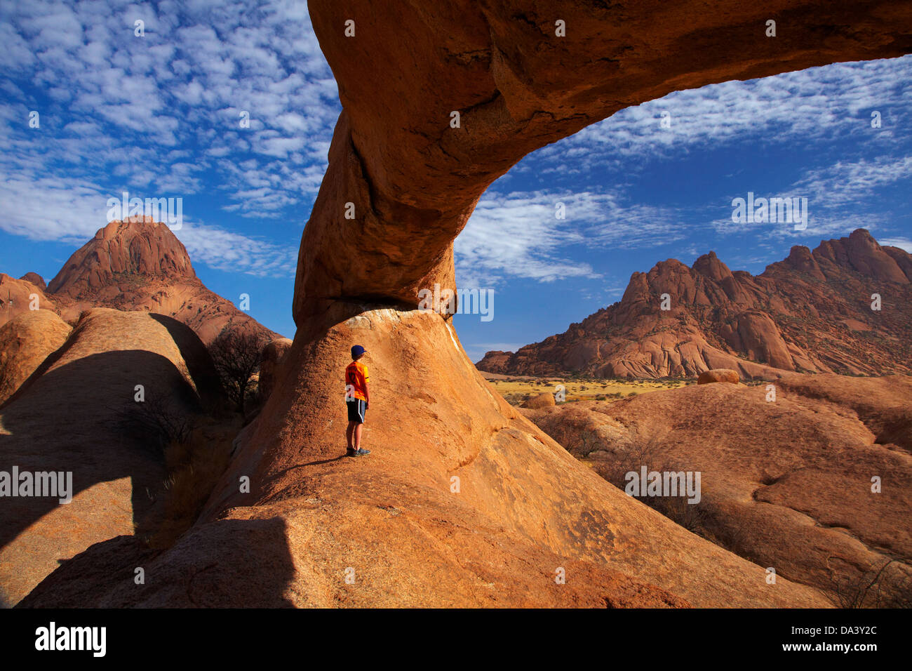 Boy under natural rock arch at Spitzkoppe (left), and Pondok Mountains in distance (right ...