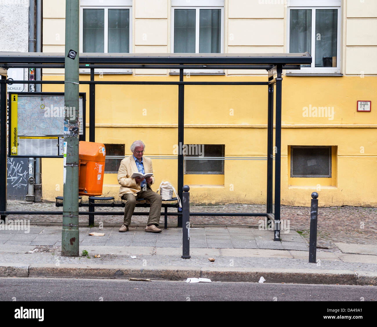 Senior man in yellow jacket reads book at bus stop with yellow wall in ...