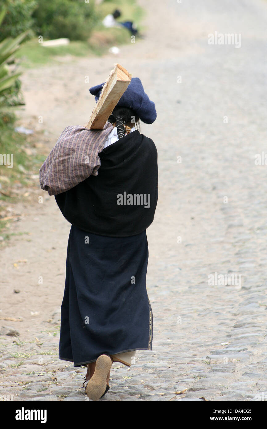 An indigenous woman carrying a log over her shoulder walks down a ...