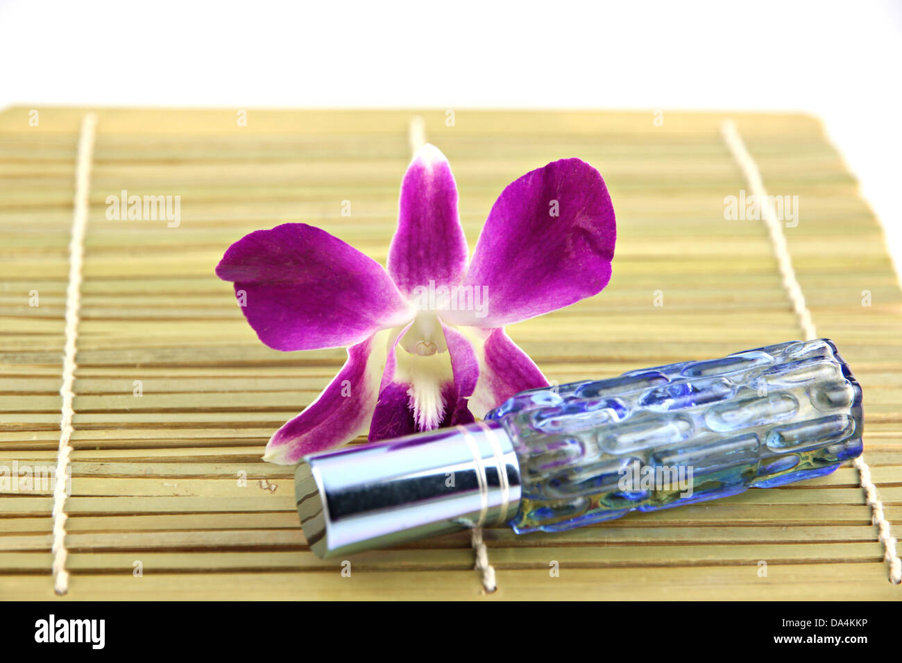 Purple orchid and blue perfume bottles in bamboo dish on white ...