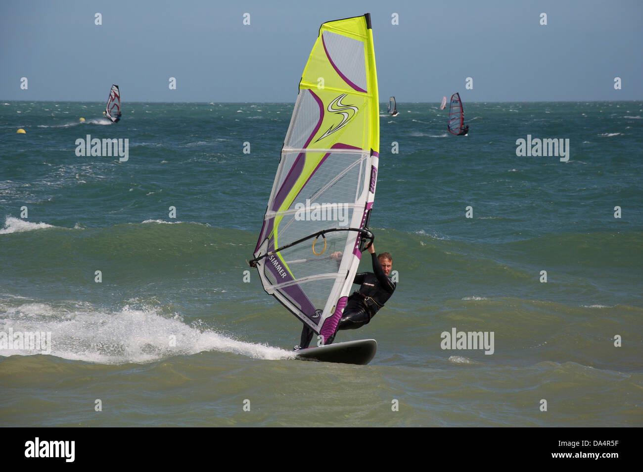 Seaside water sports. Windsurfing man, wearing a wetsuit, speeding over ...