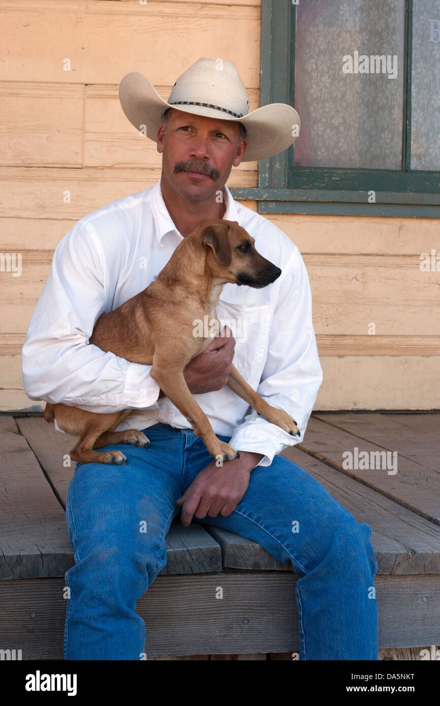 Cowboy holding his Jack Russell Terrier, sitting on the porch of an old ...