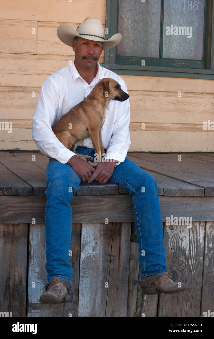 Cowboy holding his Jack Russell Terrier, sitting on the porch of an old ...