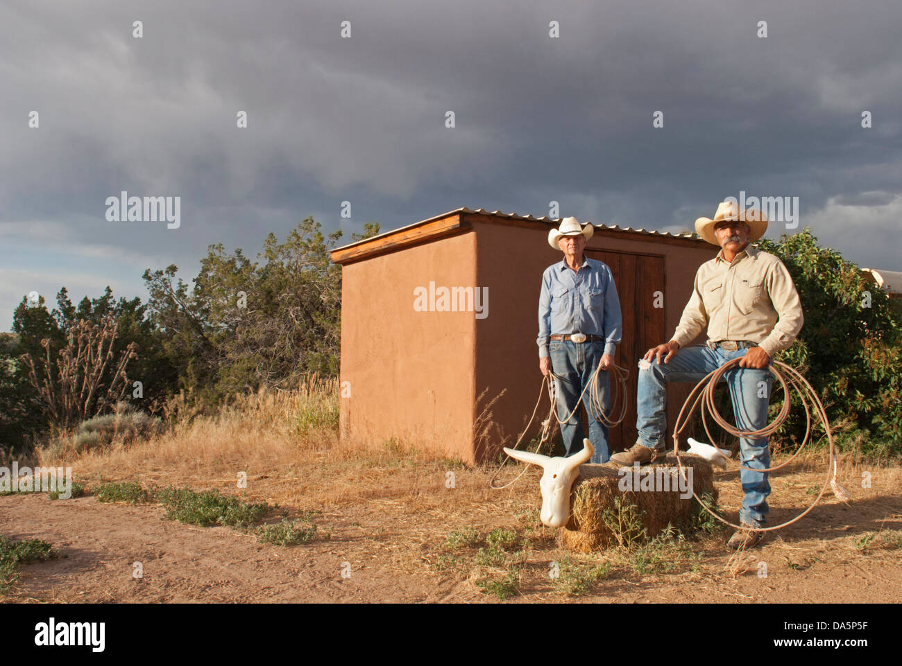Two men with lassos and roping dummy steer head attached to a hay bale ...