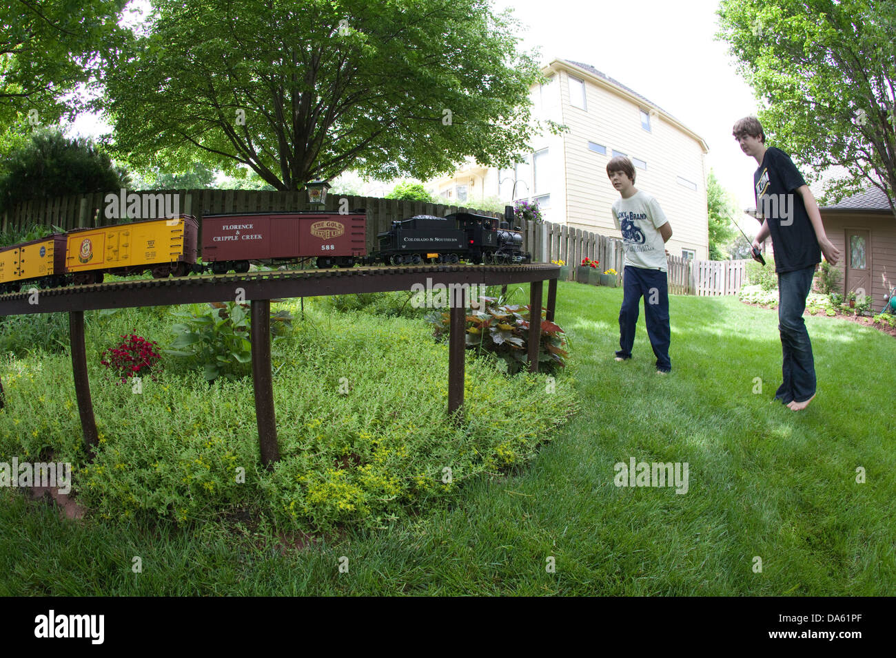 Two boys watch a miniature model train on railroad tracks, backyard ...