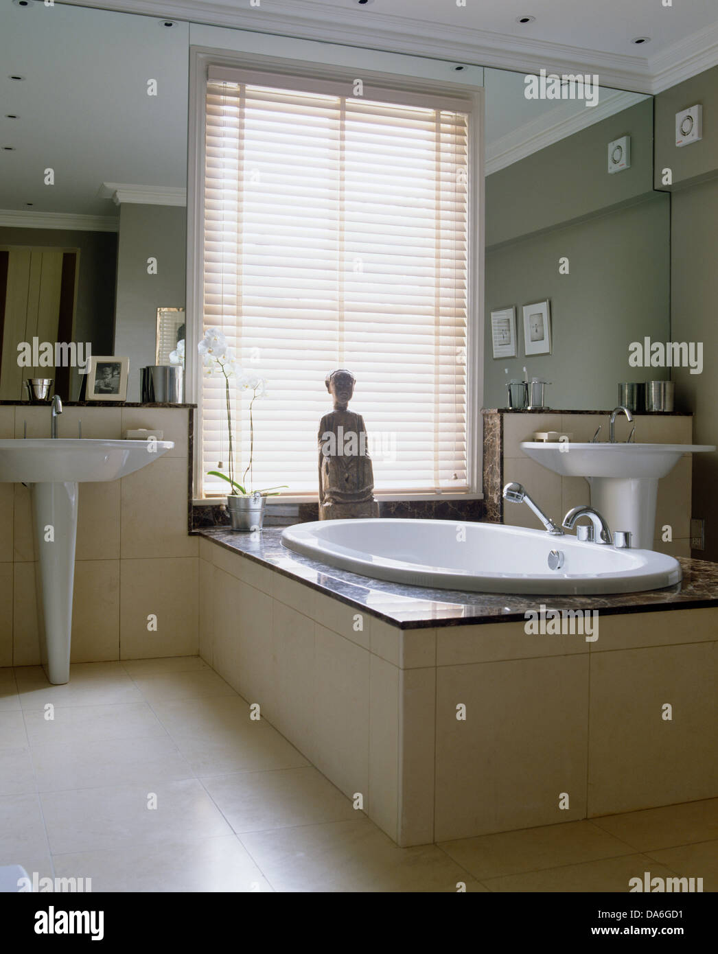 Oval bath with stone paneling below mirrored wall and window with ...
