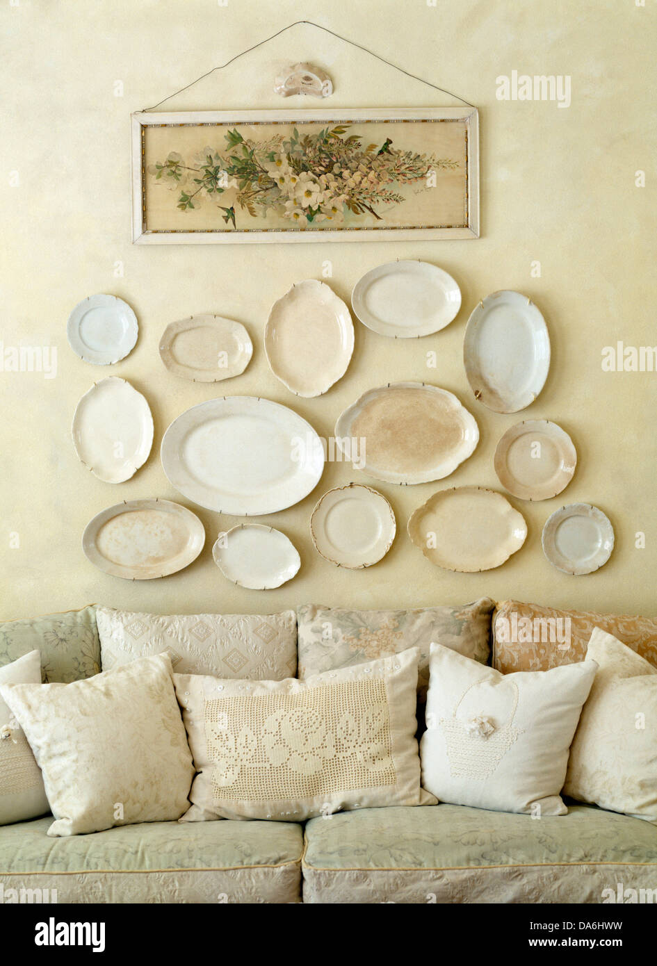 Floral sofa and collection of cream ware plates on wall above sofa with ...
