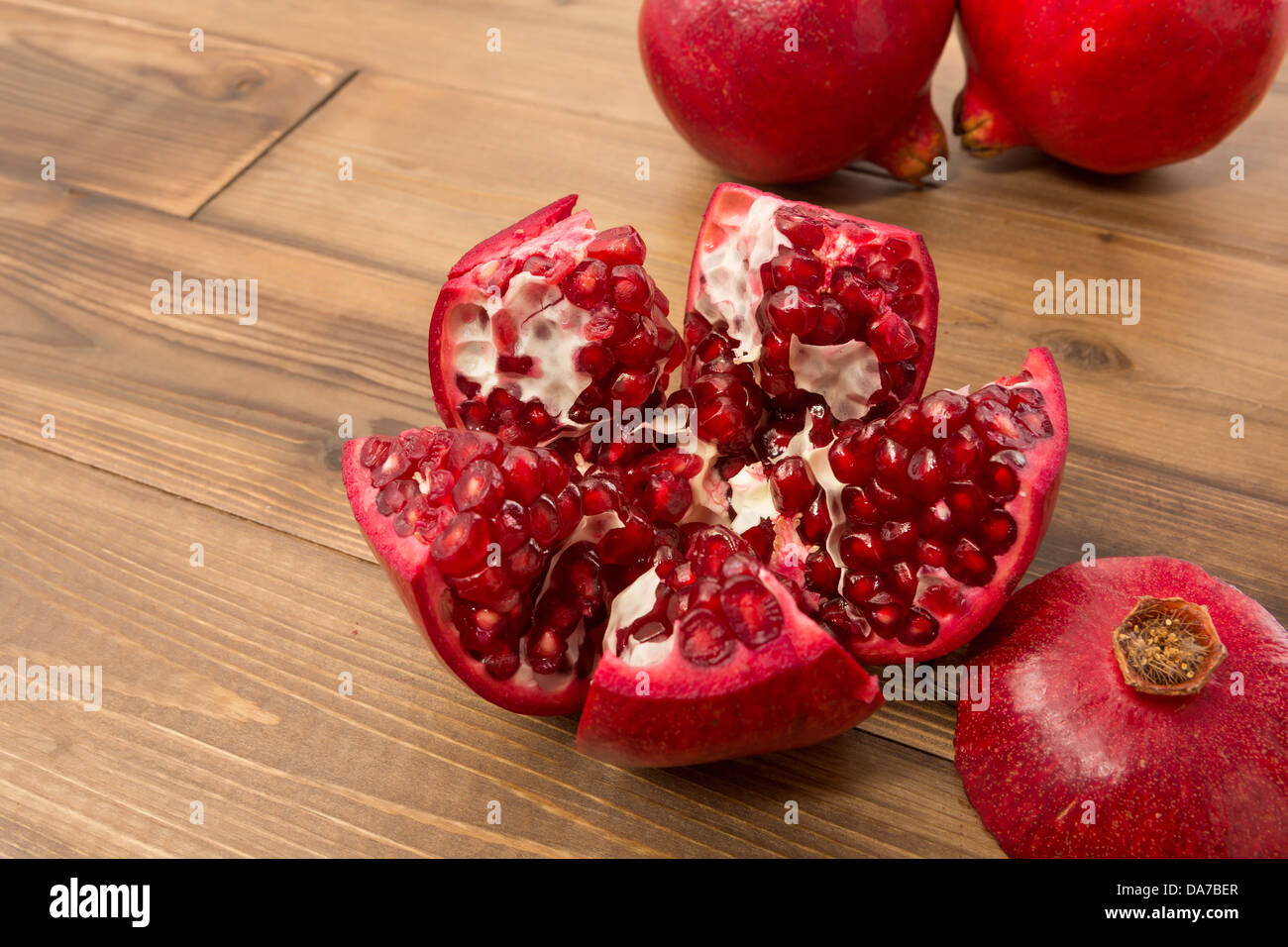 Two whole and one cut open pomegranate on a wooden table Stock Photo ...
