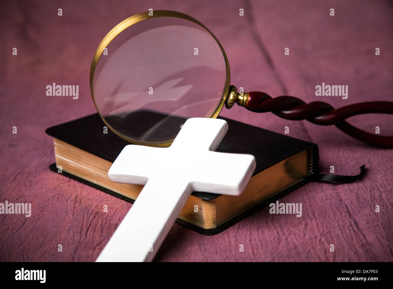 A bible, cross and magnifying glass. The cross is reflected in the ...