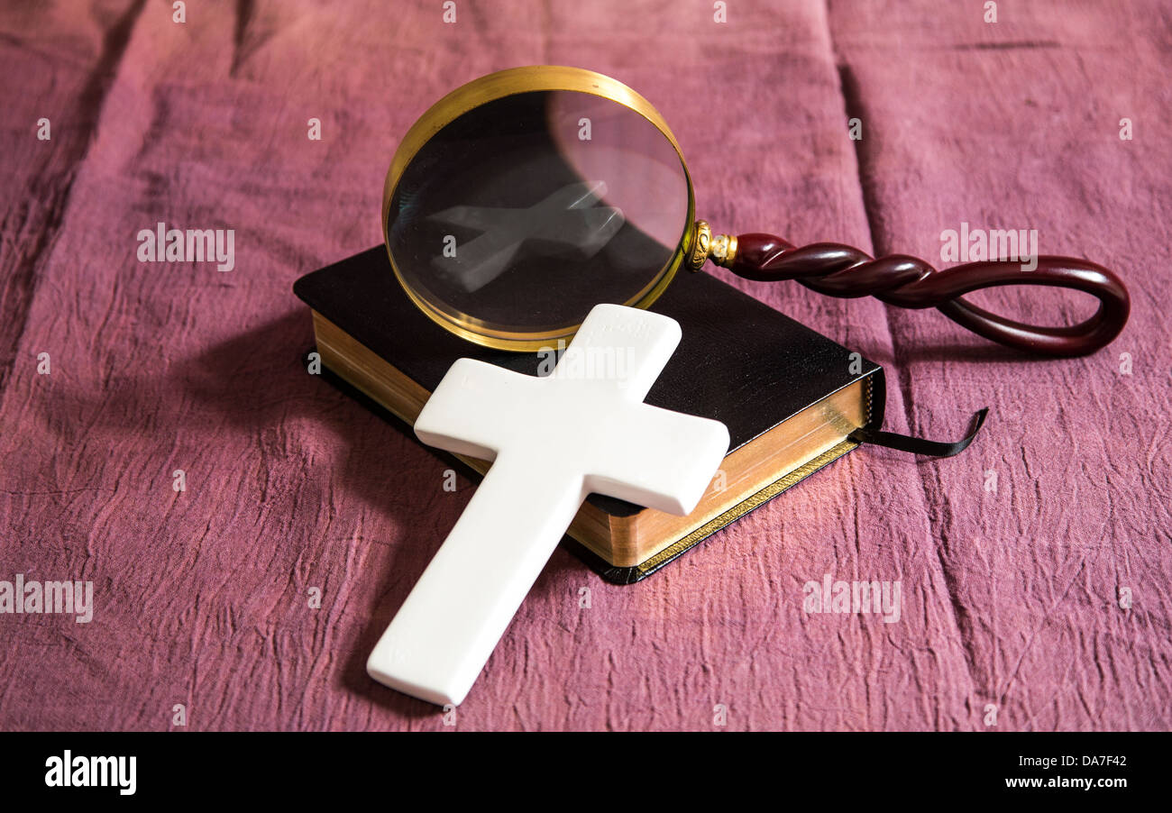 A bible, cross and magnifying glass. The cross is reflected in the ...