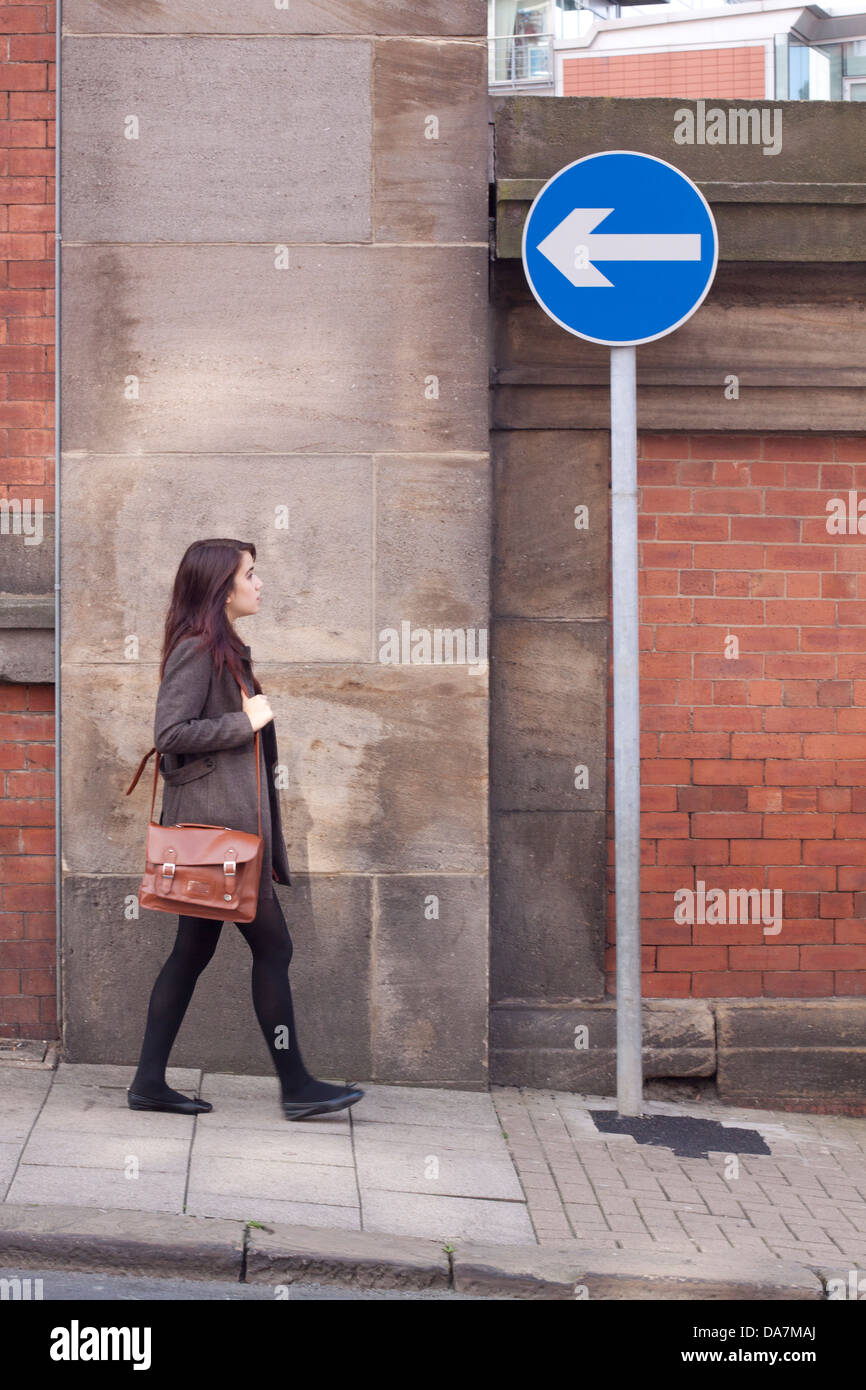 Young woman walking in the opposite direction pointed to by a one way ...