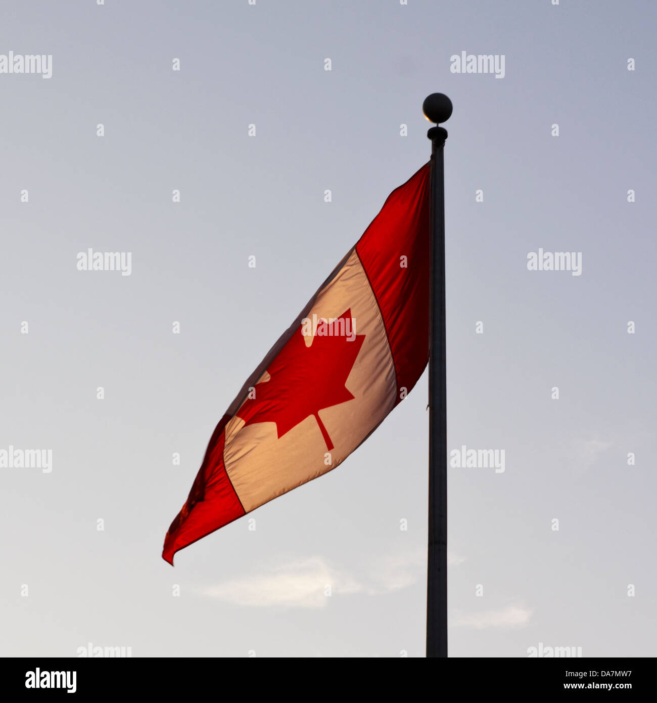 The Canadian flag, back-lit by the low sun, flying in the centre of ...