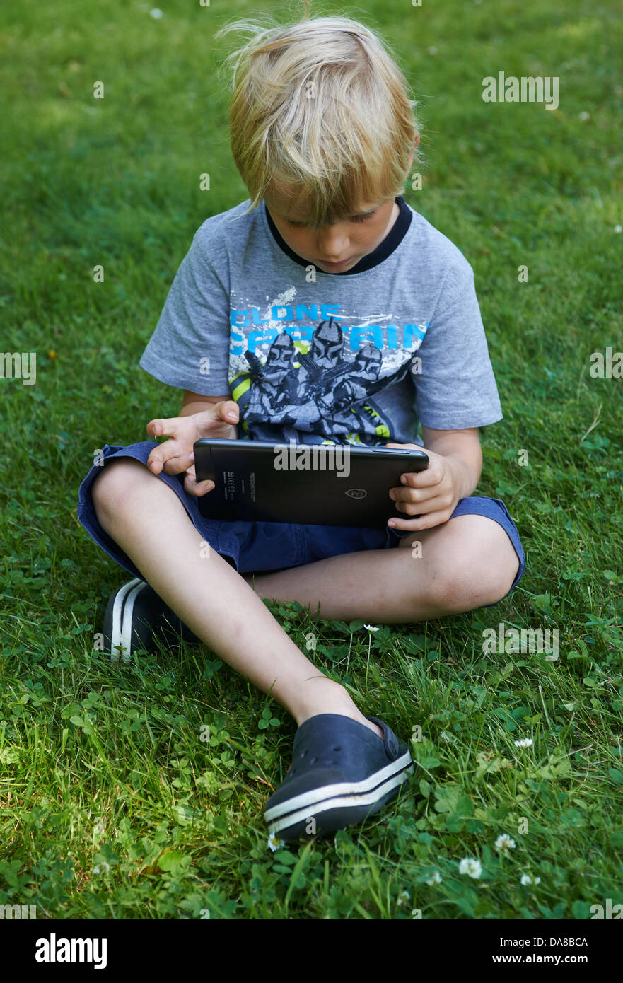 Cute child blond young boy playing with a digital tablet outdoors in ...