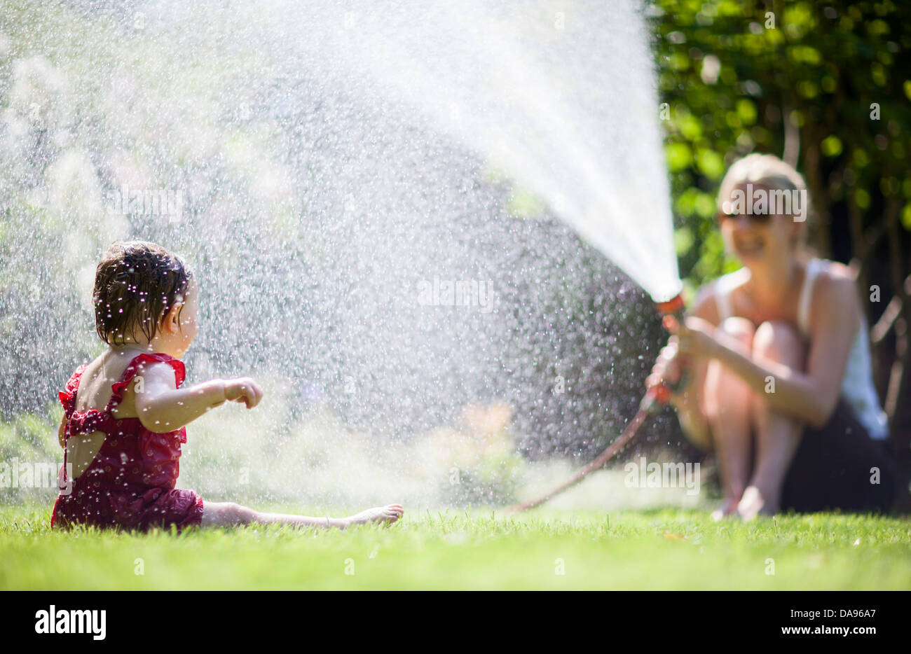 A baby squeals in delight as she is cooled down by mum spraying water ...