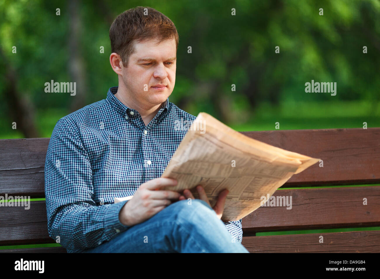 Man reads newspaper on bench in the park Stock Photo - Alamy