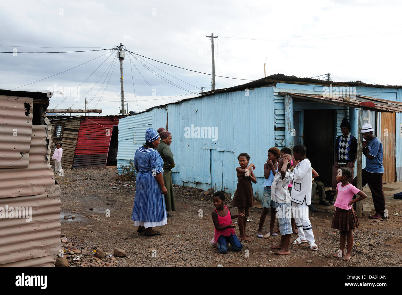 Group of children standing in front of shacks talking to adults at ...