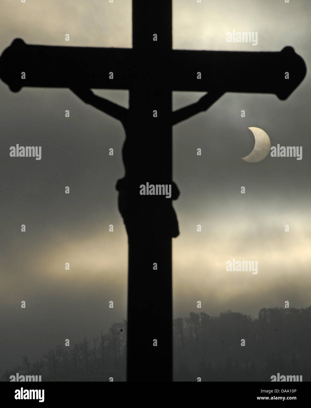 The sun appears sickle-shaped next to a cross during a partial solar ...