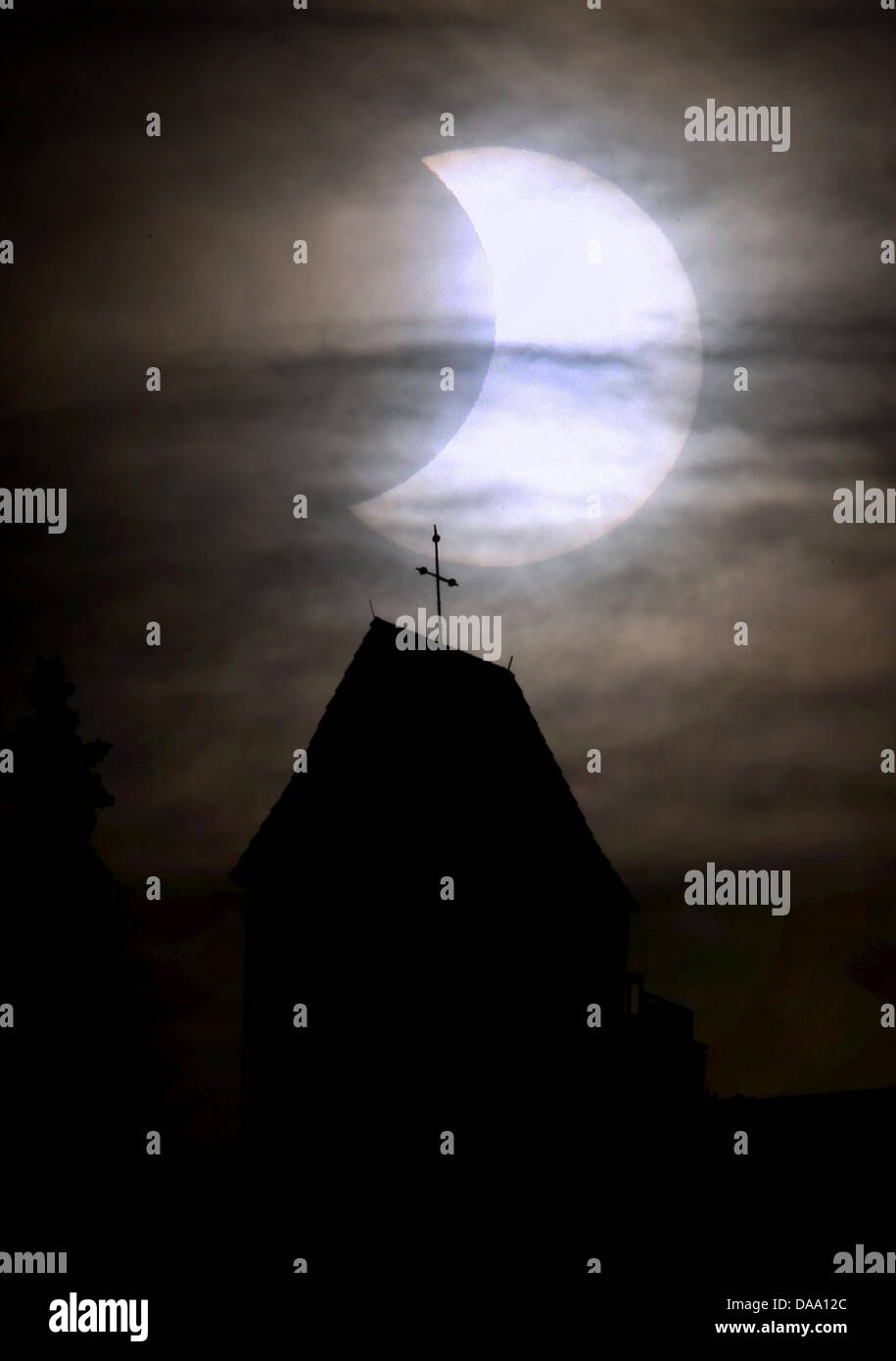 The sun appears sickle-shaped behind a church during a partial solar ...