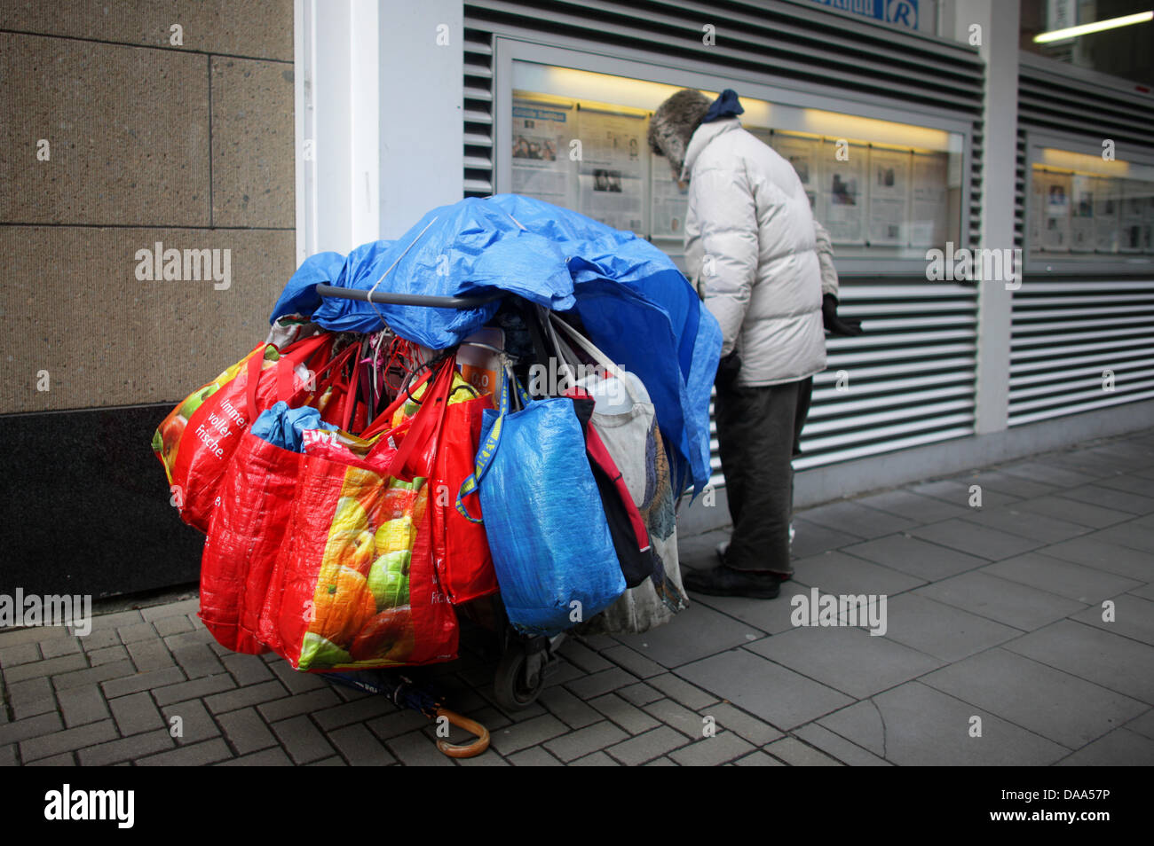 A homeless person with his belongings reads the news at the window of a ...