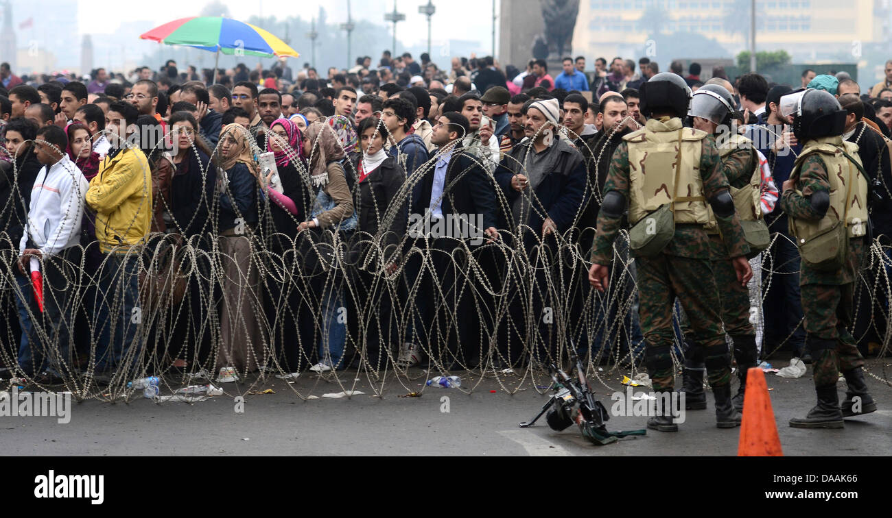 Protesters gather behind a gap in a barbed wire barricade in a street ...