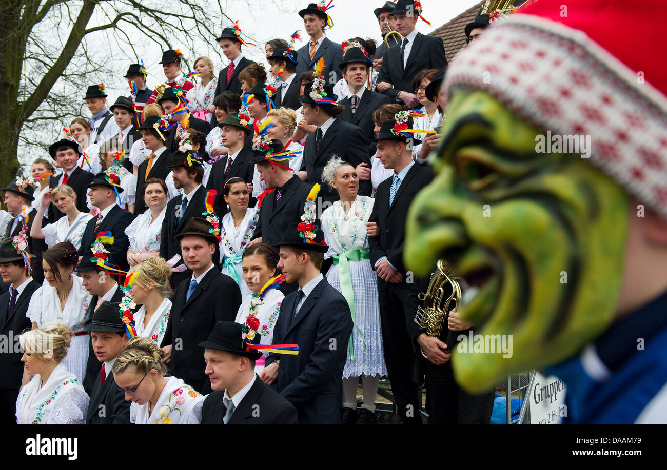 A man wearing a green fools mask stands next to a crowd of men and ...