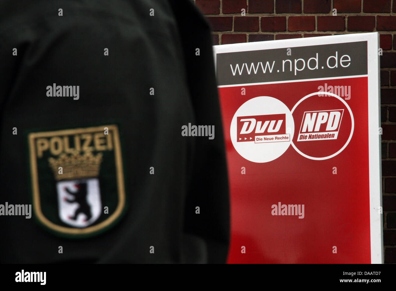 A sign with the logos of the NPD and DVU and a police officer stand at ...