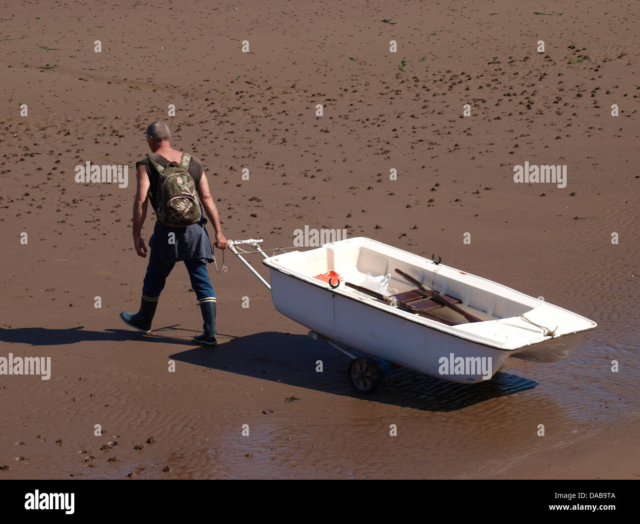 Man pulling rowing boat on a trolley across the beach, Somerset, UK ...