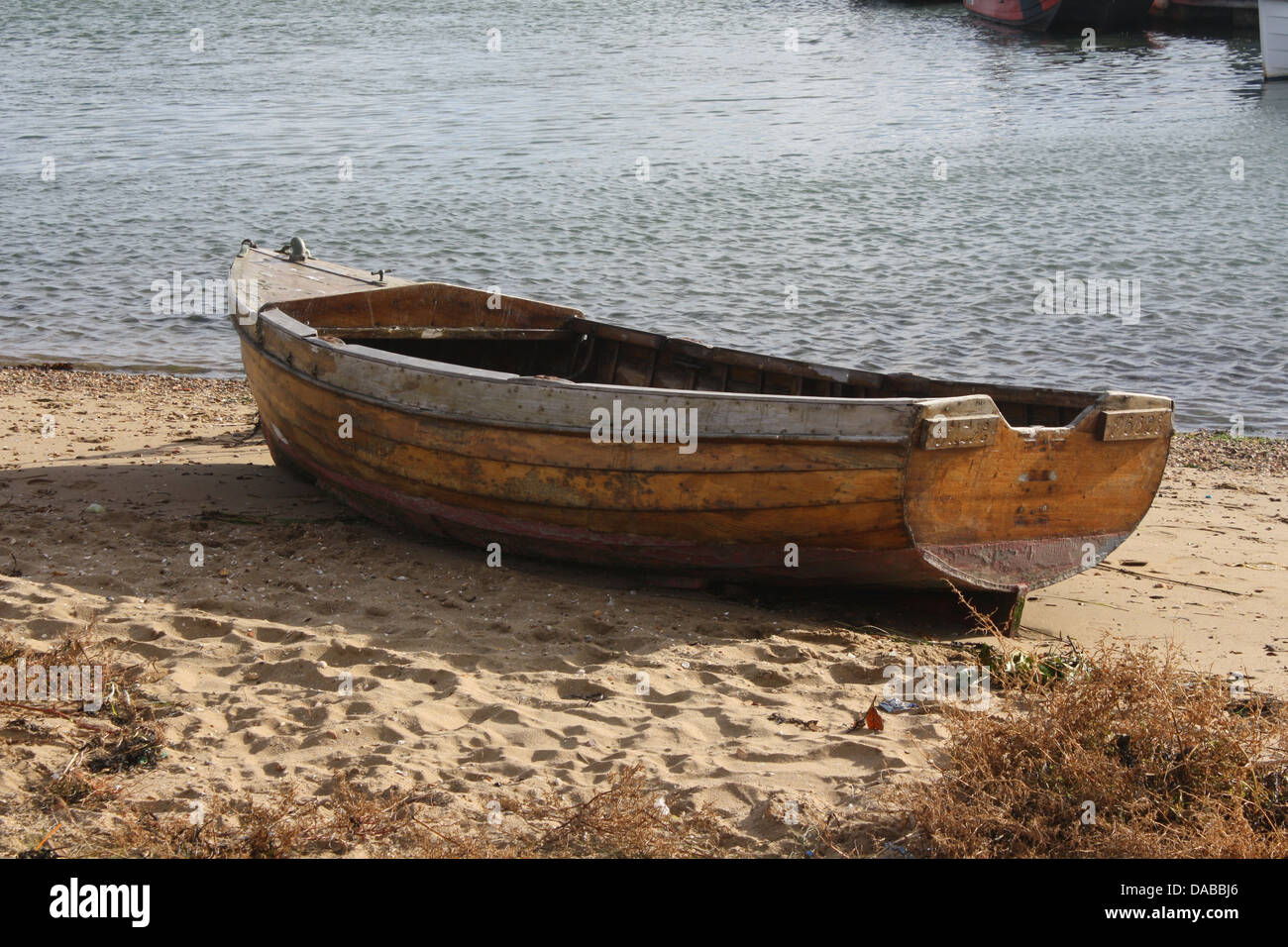 Old wooden clinker rowing boat pulled out of the water and sat on sandy ...
