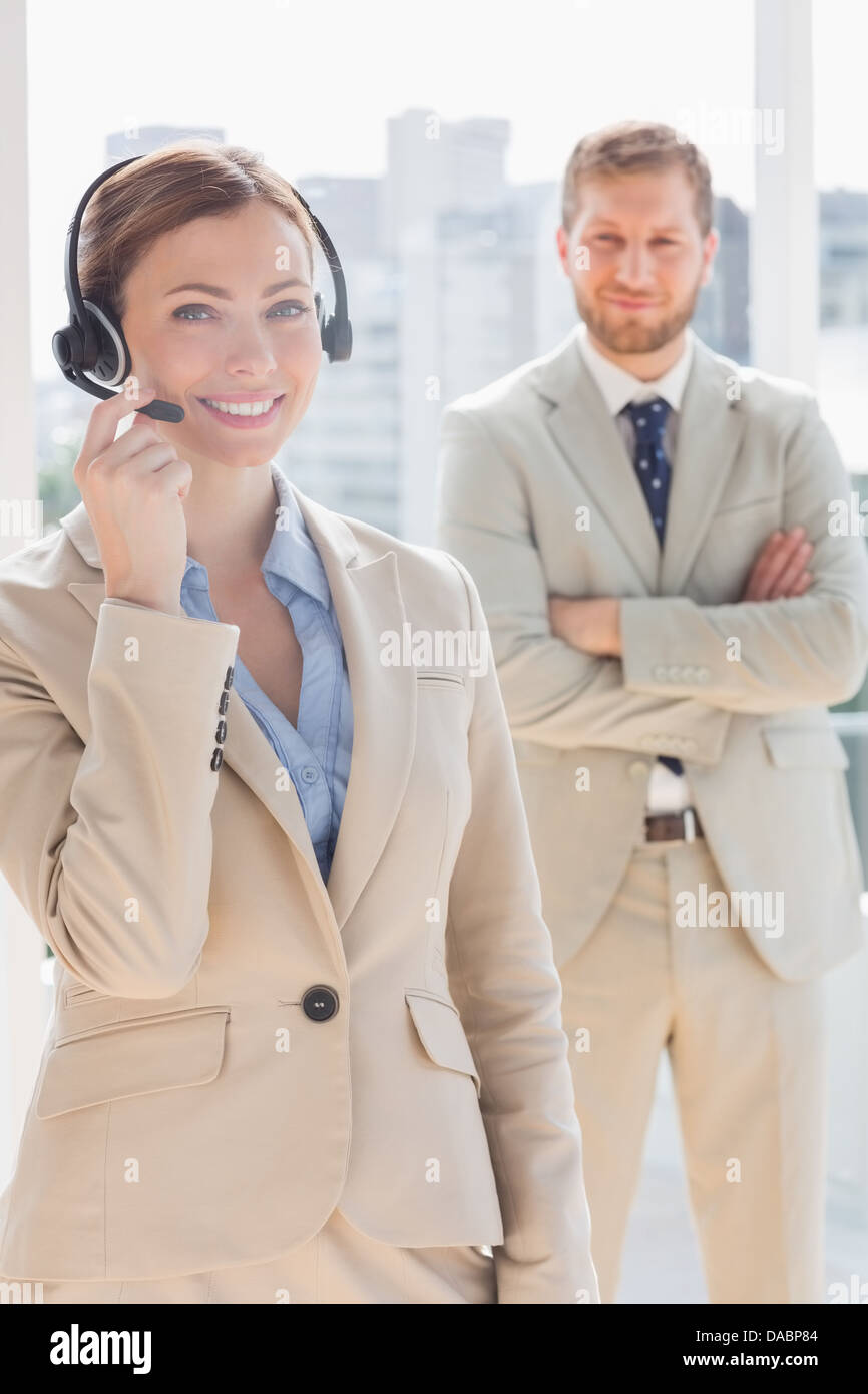 Pretty call centre agent with colleague behind her Stock Photo - Alamy