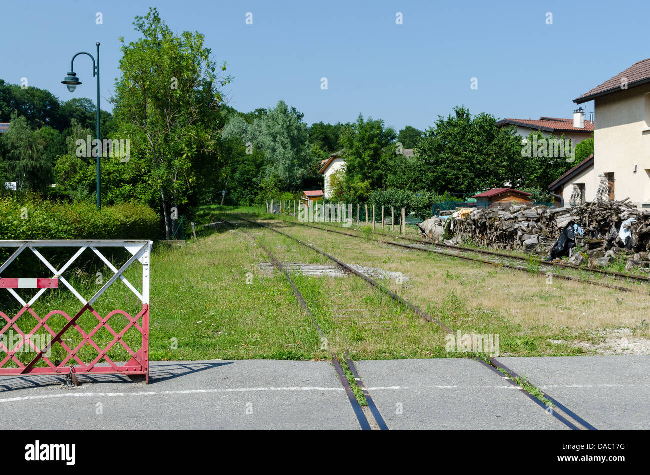 Overgrown railway tracks cross a road at a level crossing in the French ...
