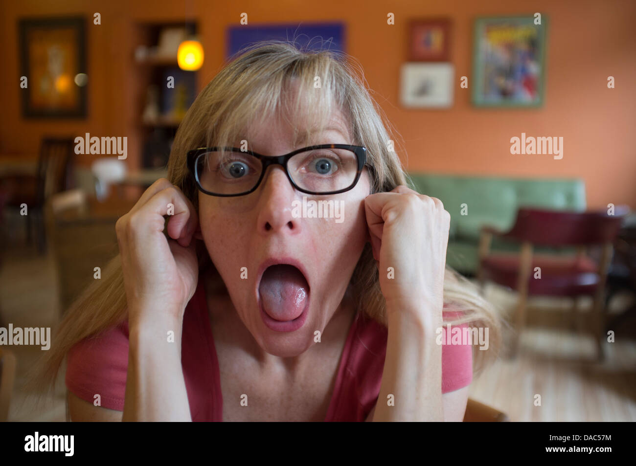 Woman Wearing Glasses Sticking Tongue Out And Holding Ears With Eyes