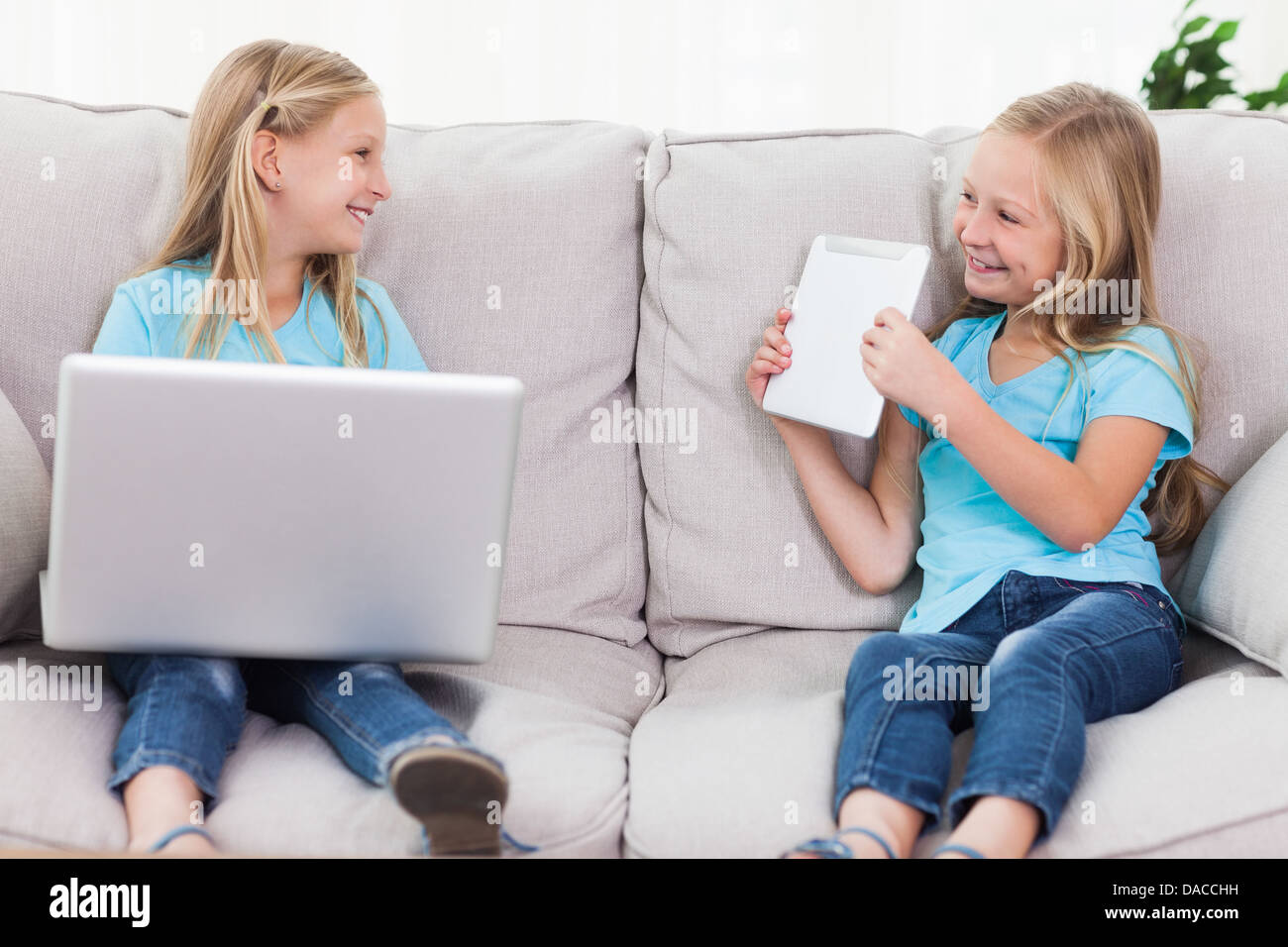 Young twins using a laptop and a tablet sitting on a couch Stock Photo ...