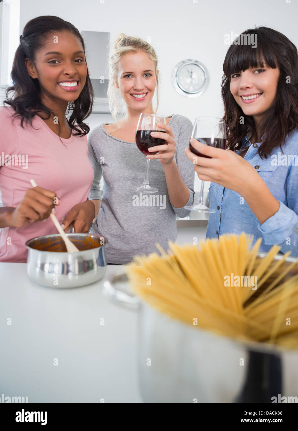 Happy friends making spaghetti dinner together and drinking red wine ...