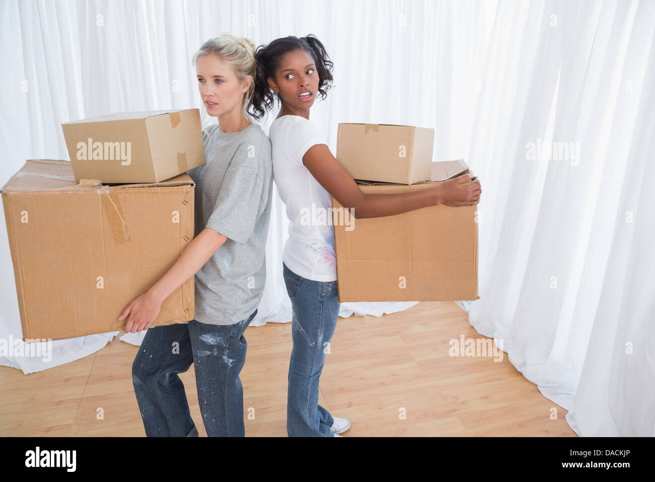 Friends standing back to back holding moving boxes Stock Photo - Alamy