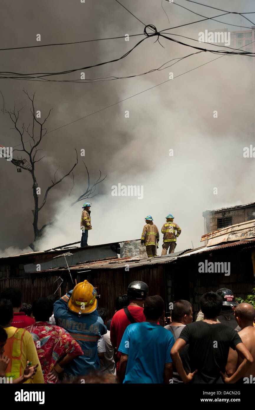Crowd watch firemen hose down a fire in a shanty town in Makati City ...