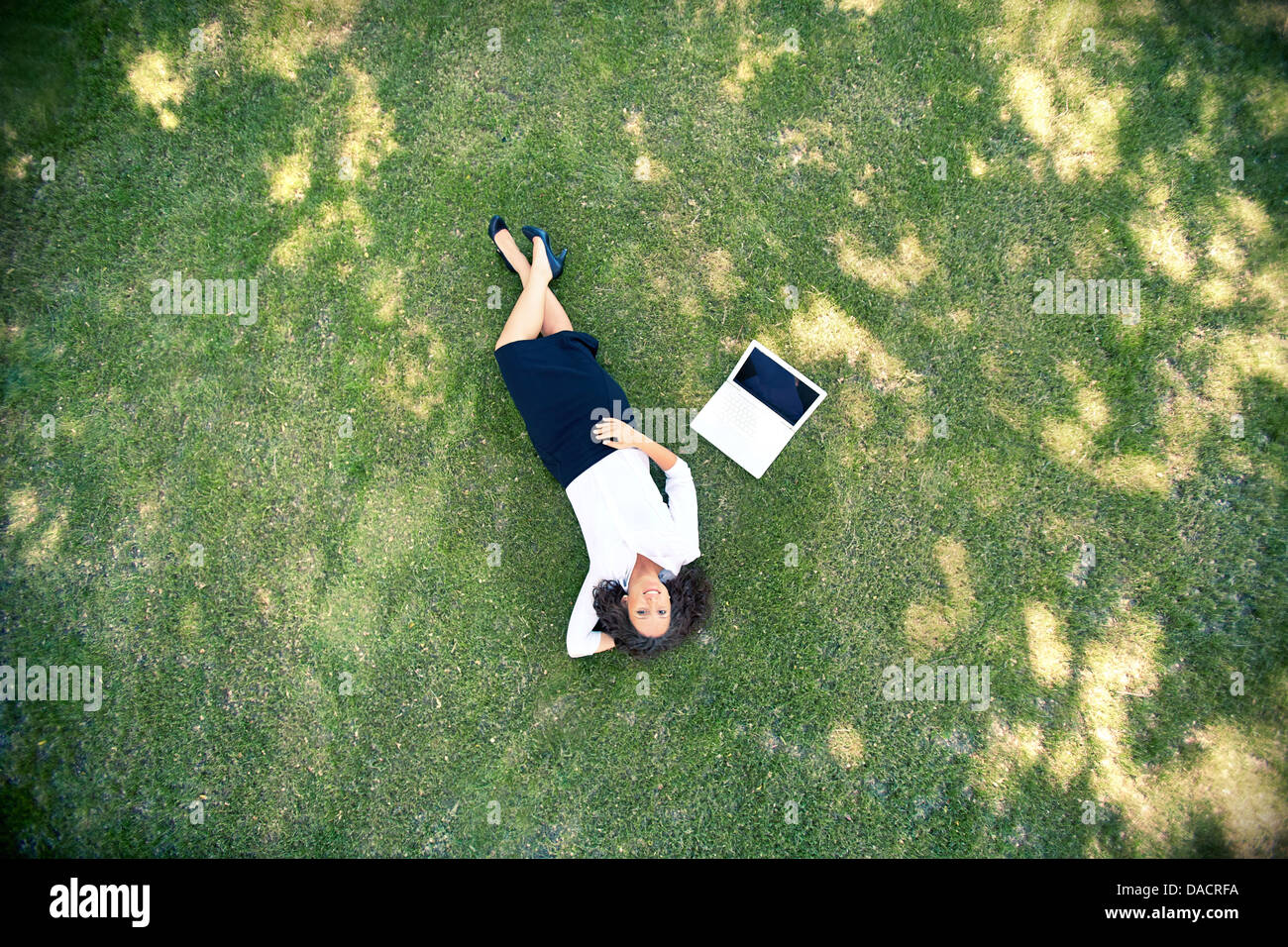 Above view of successful businesswoman lying on green grass with laptop ...